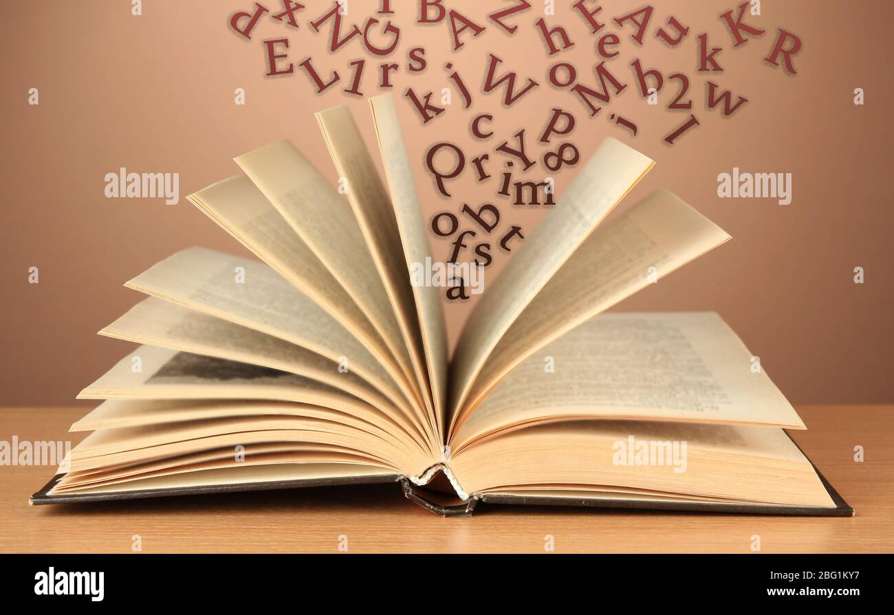 Opened book with letters flying out of it on brown background Stock ...