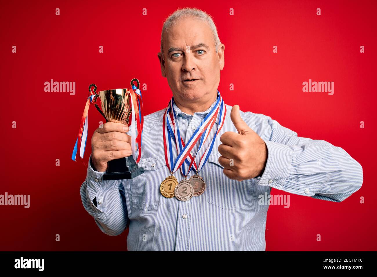 Middle age hoary successful man wearing medals holding trophy over ...