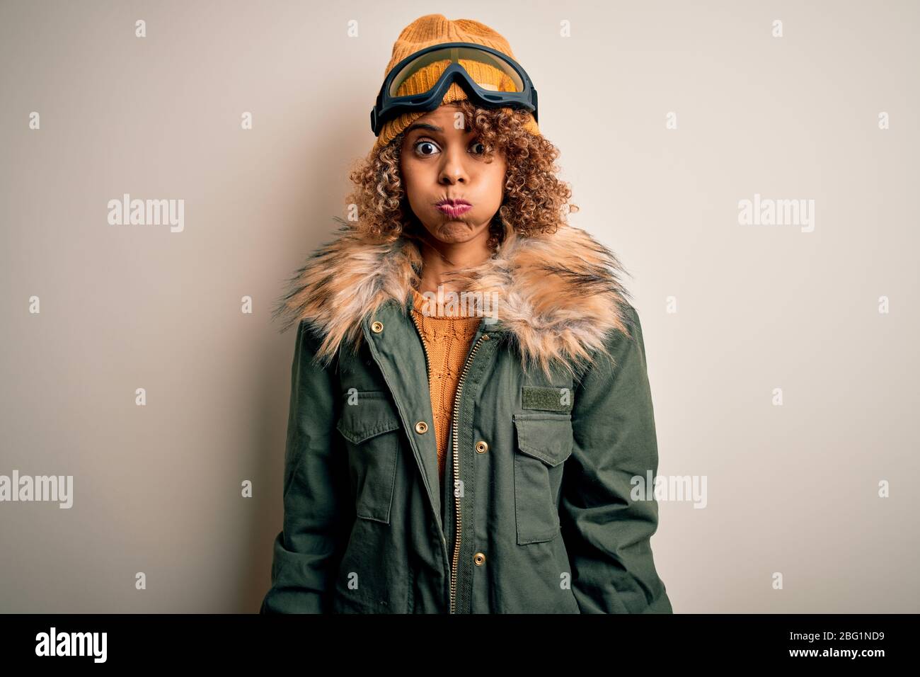 Young african american skier woman with curly hair wearing snow sportswear and ski goggles ...