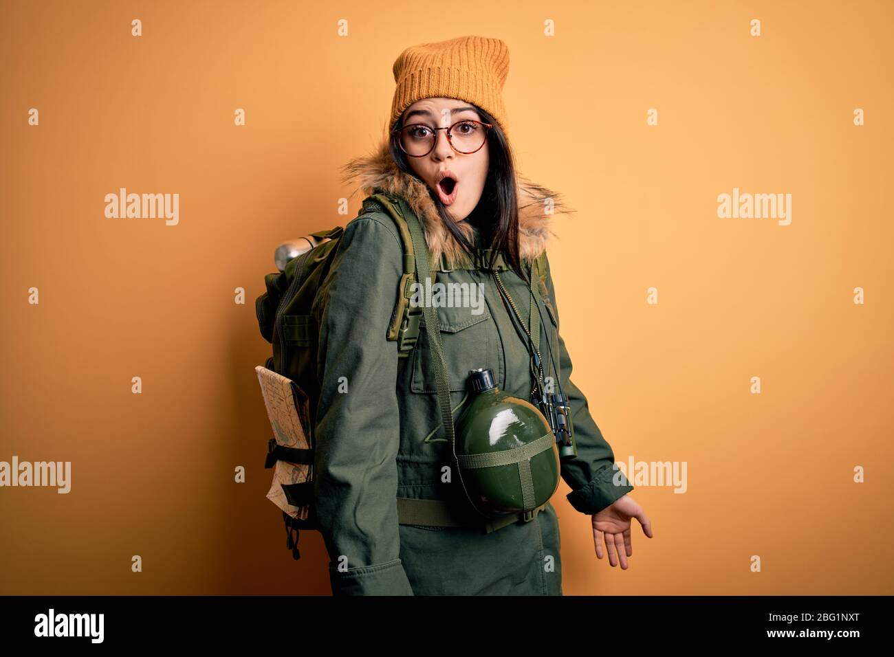 Young hiker woman wearing hiking backpack, canteen and map over yellow ...