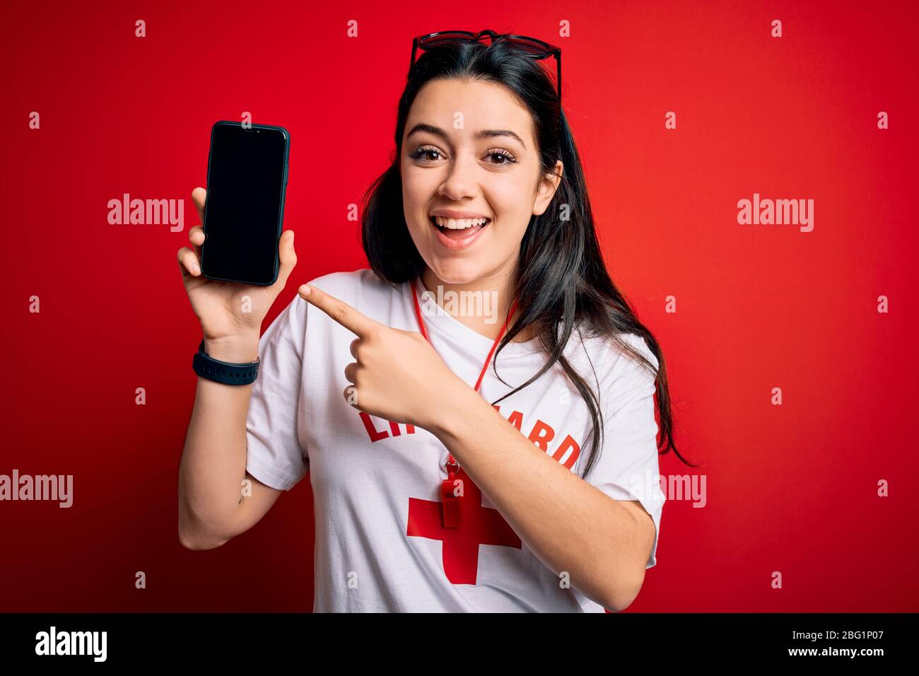 Young lifeguard woman showing smartphone screen over red background ...