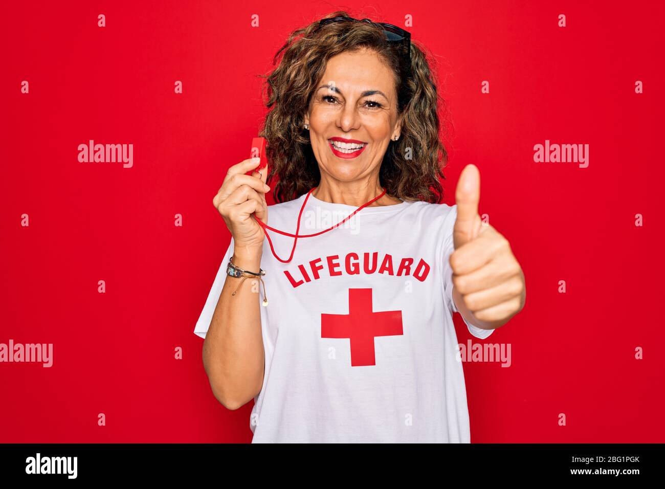 Middle age senior summer lifeguard woman holding whistle over red ...