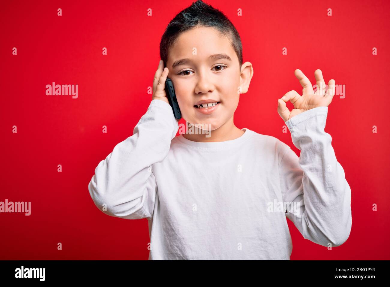 Young little boy kid talking on smartphone mobile over red isolated ...