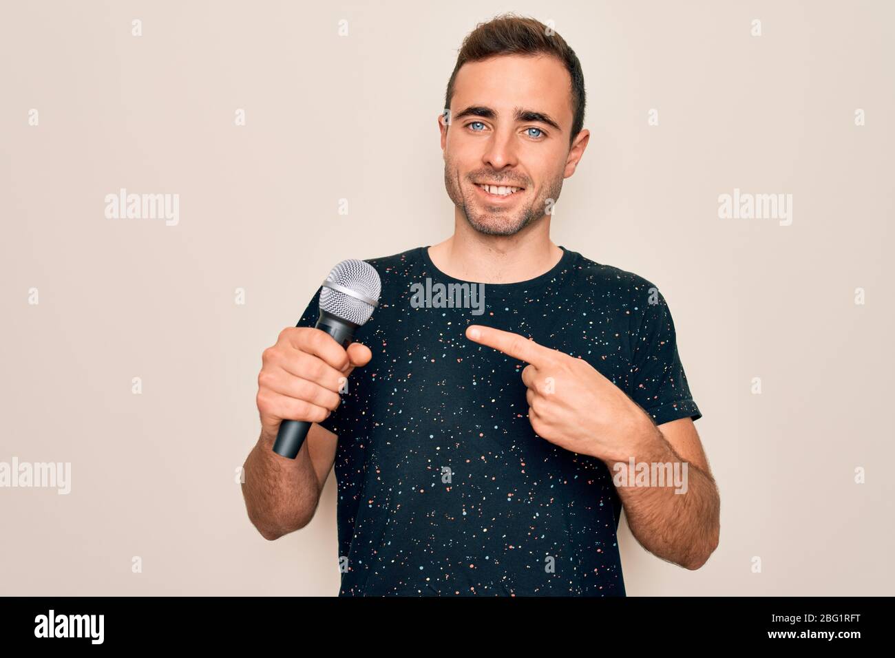 Young handsome singer man with blue eyes singing using microphone over white background very ...