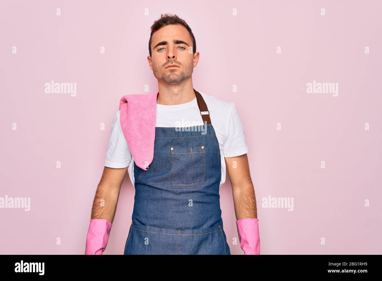 Young cleaner man with blue eyes cleaning wearing apron and gloves over ...