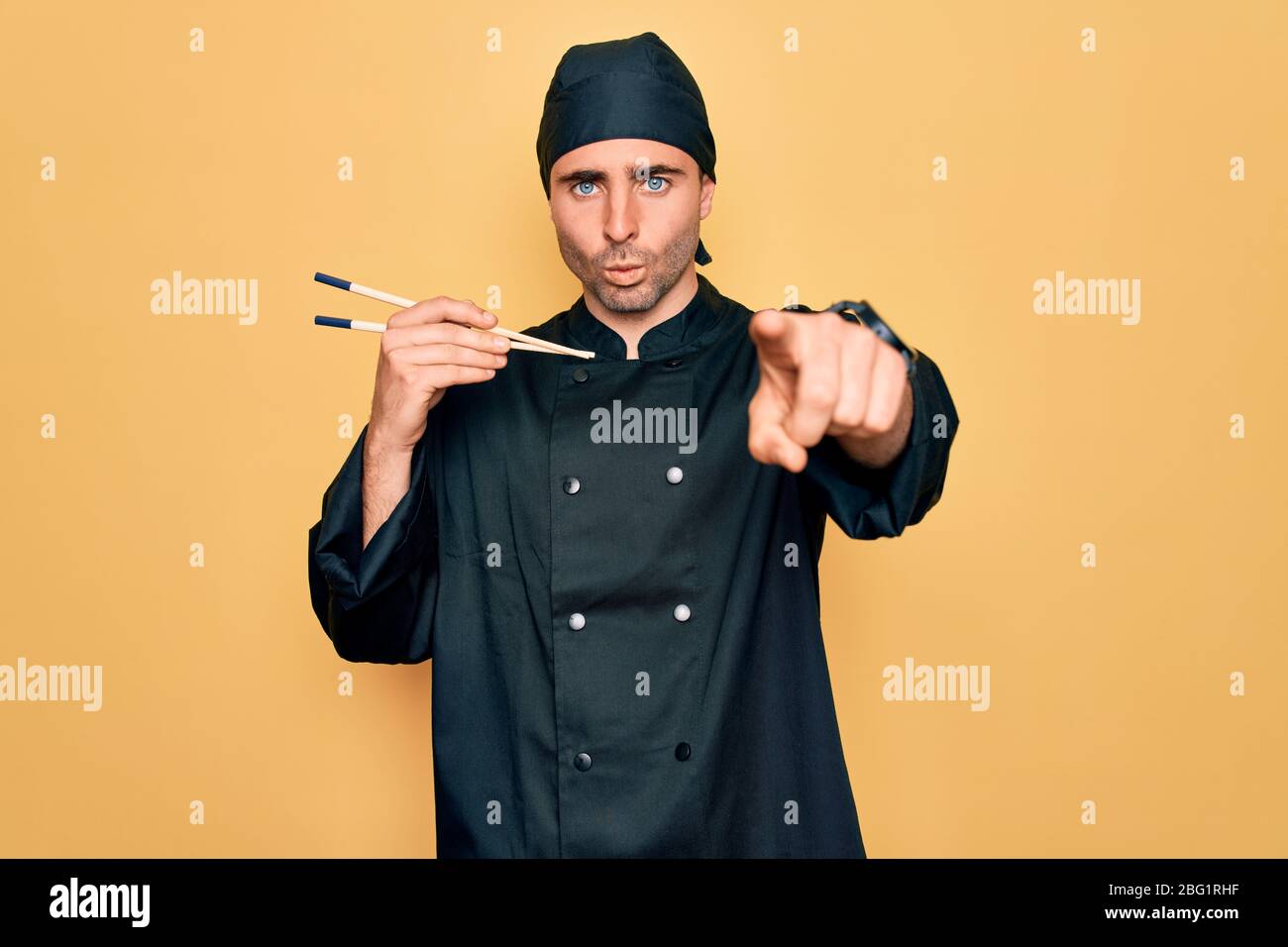 Young handsome cooker man with blue eyes wearing uniform and hat using ...