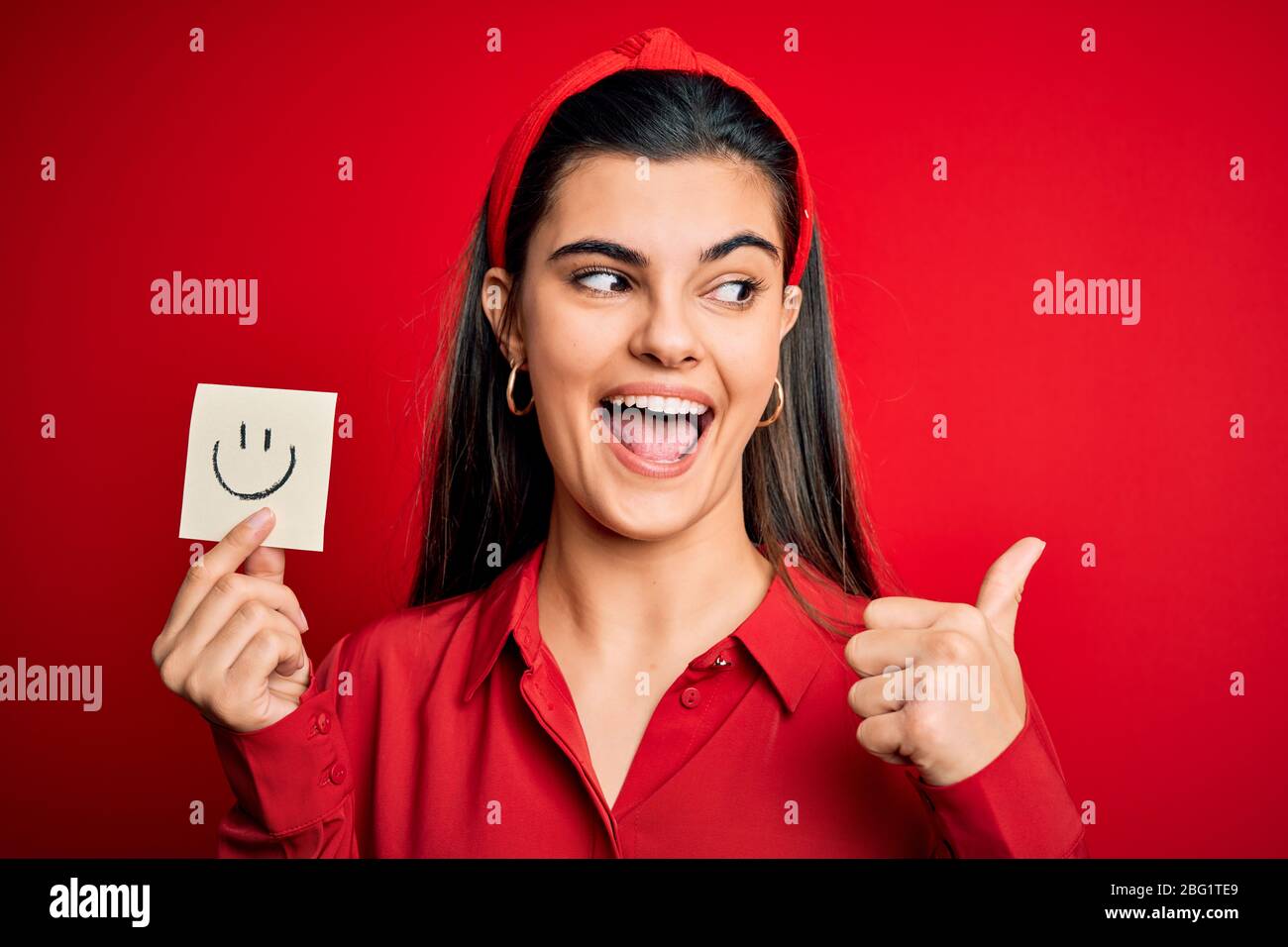 Young beautiful brunette woman holding reminder paper with smile emoji ...
