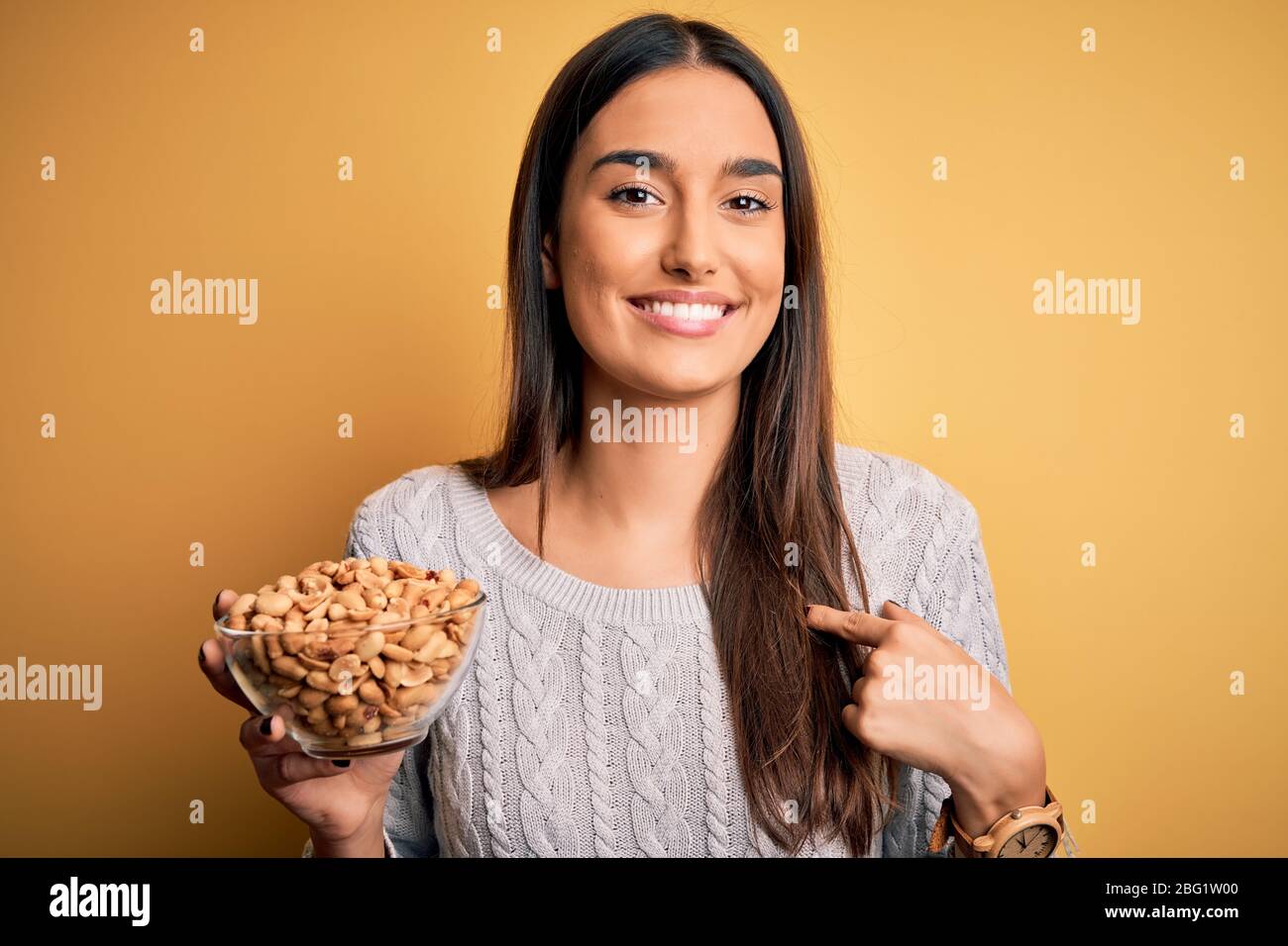 Young beautiful brunette woman holding bowl with peanuts over isolated ...