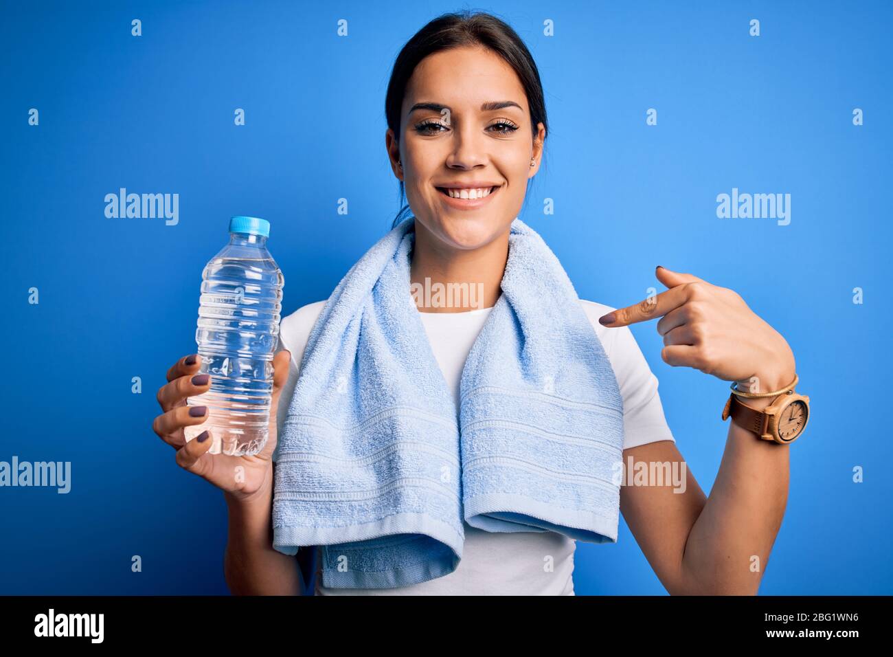 Young beautiful brunette sportswoman wearing towel drinking bottle of ...