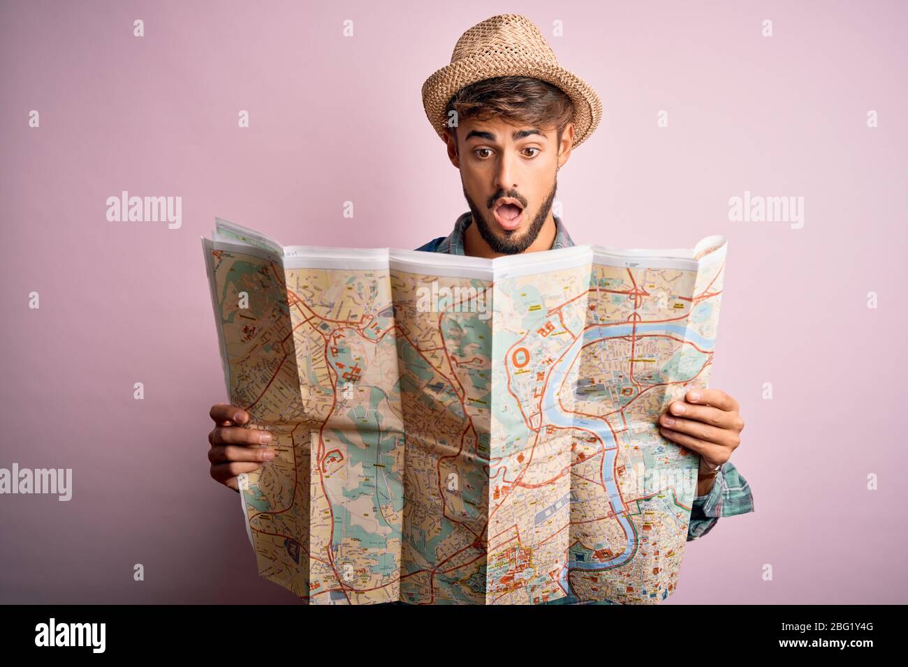 Young tourist man on vacation wearing hat holding city map standing ...