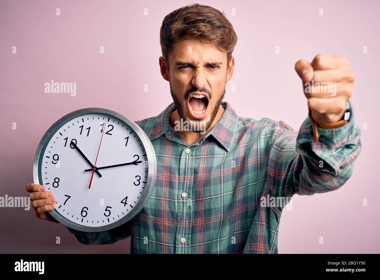 Young man with beard doing countdown using big clock over isolated pink ...