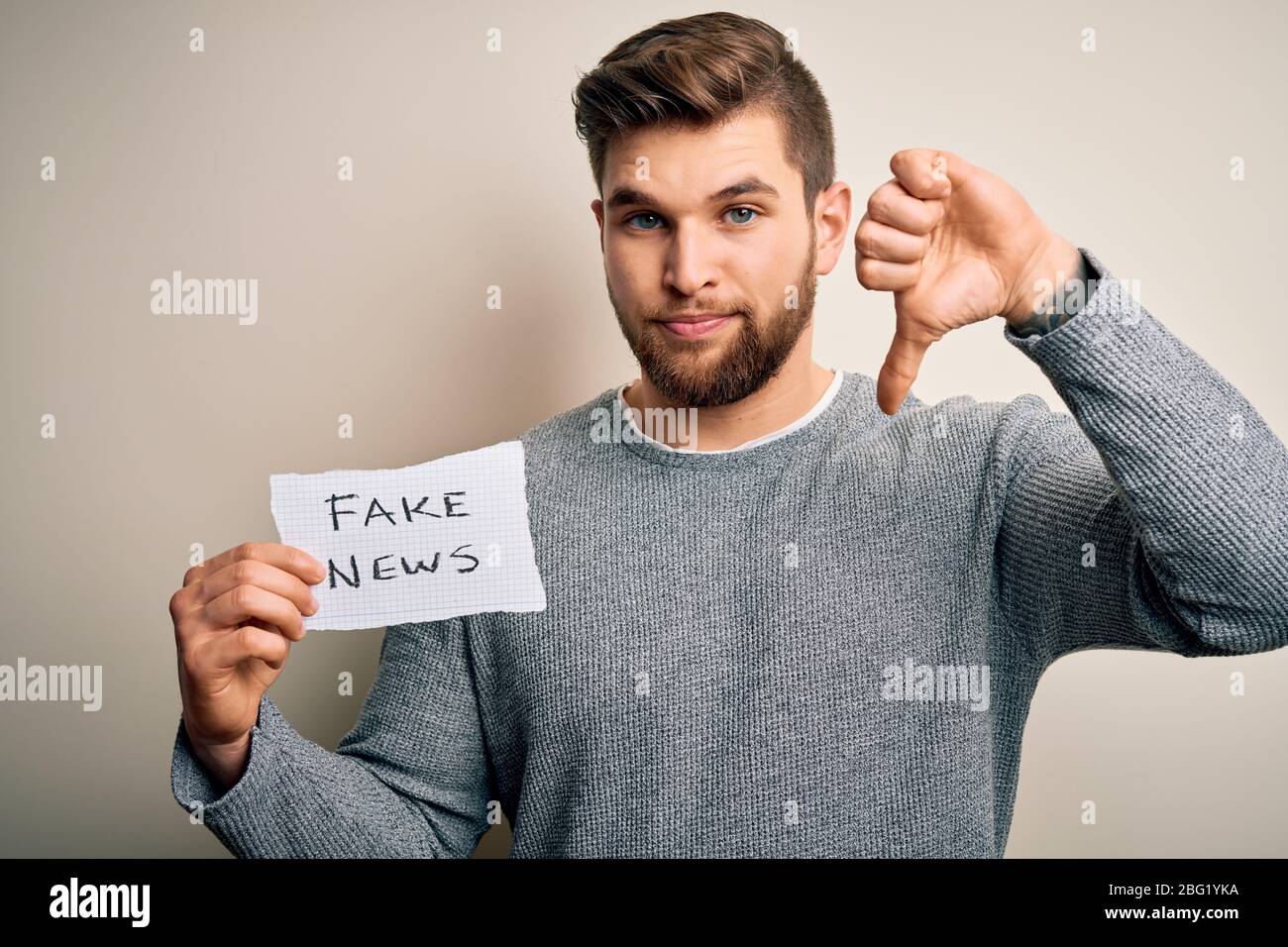 Young blond man with beard and blue eyes holding paper with fake news ...