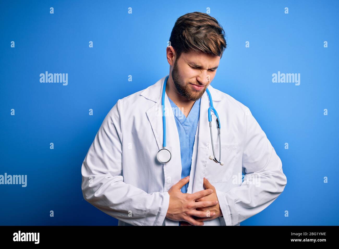 Young blond doctor man with beard and blue eyes wearing white coat and ...