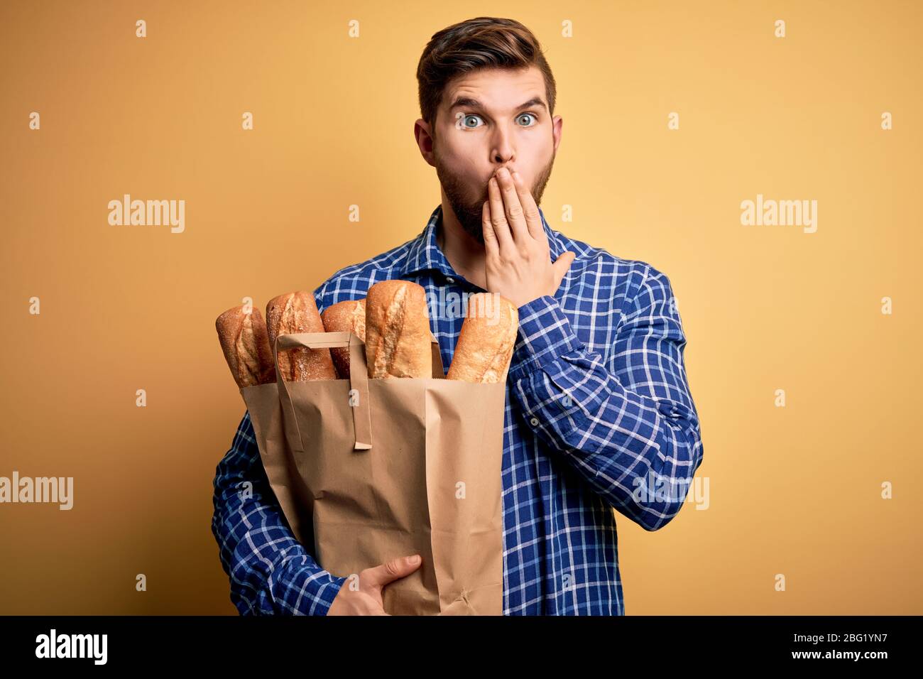 Young blond man with beard and blue eyes holding paper bag with bread ...