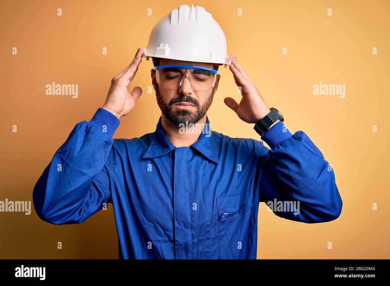 Mechanic man with beard wearing blue uniform and safety glasses over ...