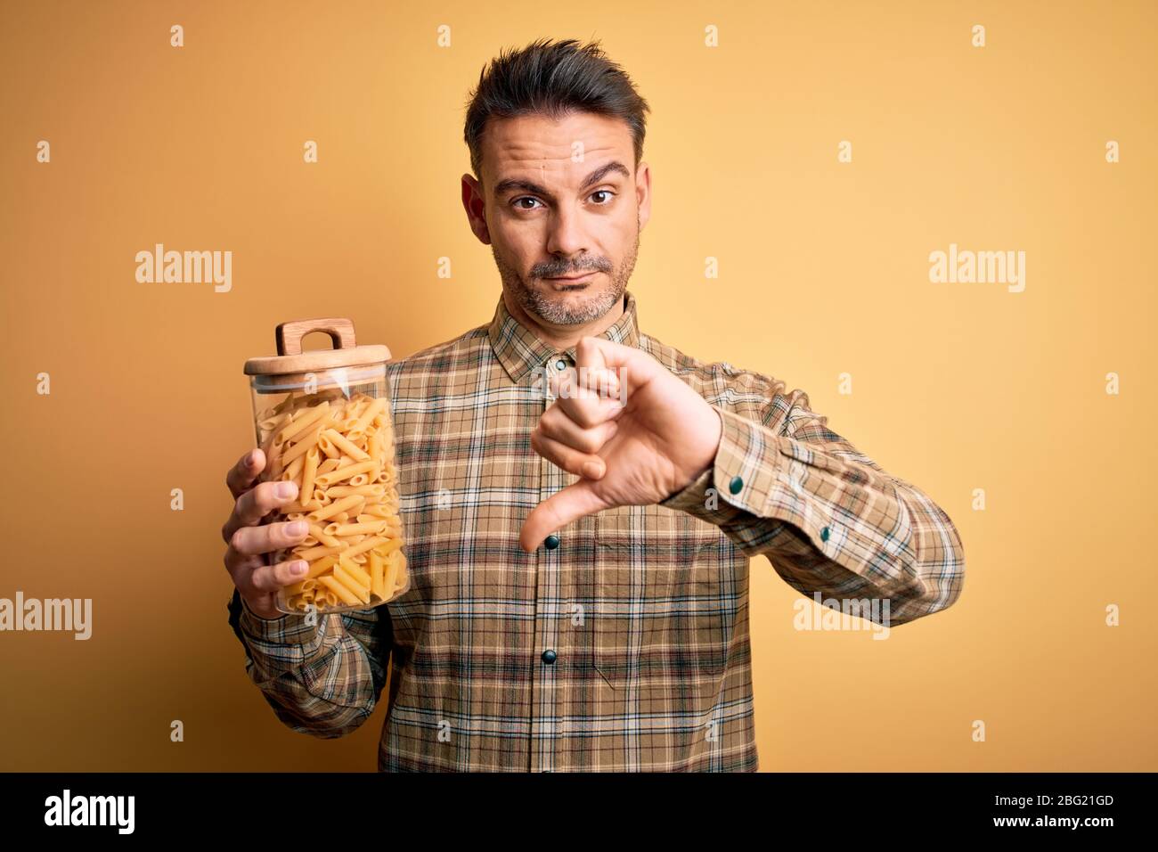 Young handsome man holding jar with dry italian pasta macaroni over ...