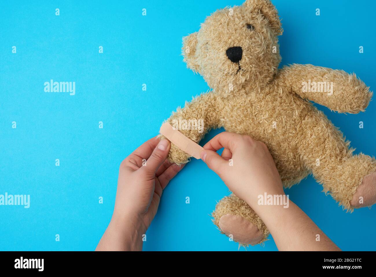 two hands holding a teddy bear and gluing an adhesive plaster on a paw ...