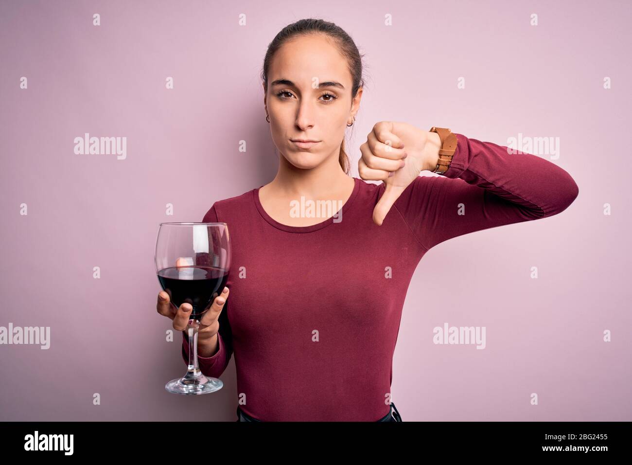 Young beautiful woman drinking glass with red wine over isolated pink ...