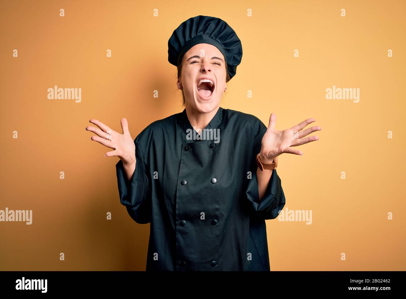 Young beautiful chef woman wearing cooker uniform and hat standing over ...