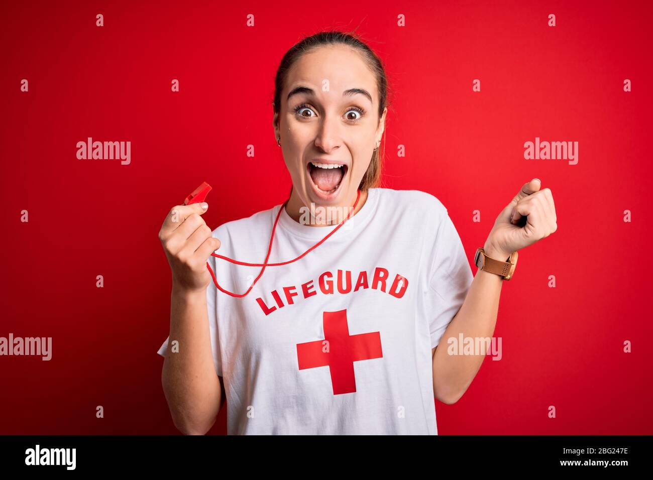 Beautiful lifeguard woman wearing t-shirt with red cross using whistle ...