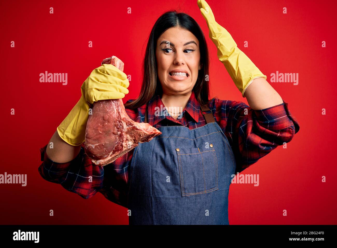 Young butcher woman holding fresh raw beef meat stake over red ...