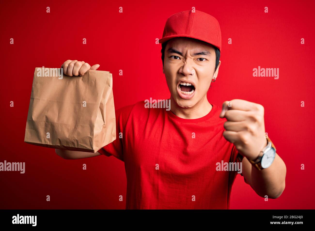 Young handsome chinese delivery man holding takeaway paper bag with ...