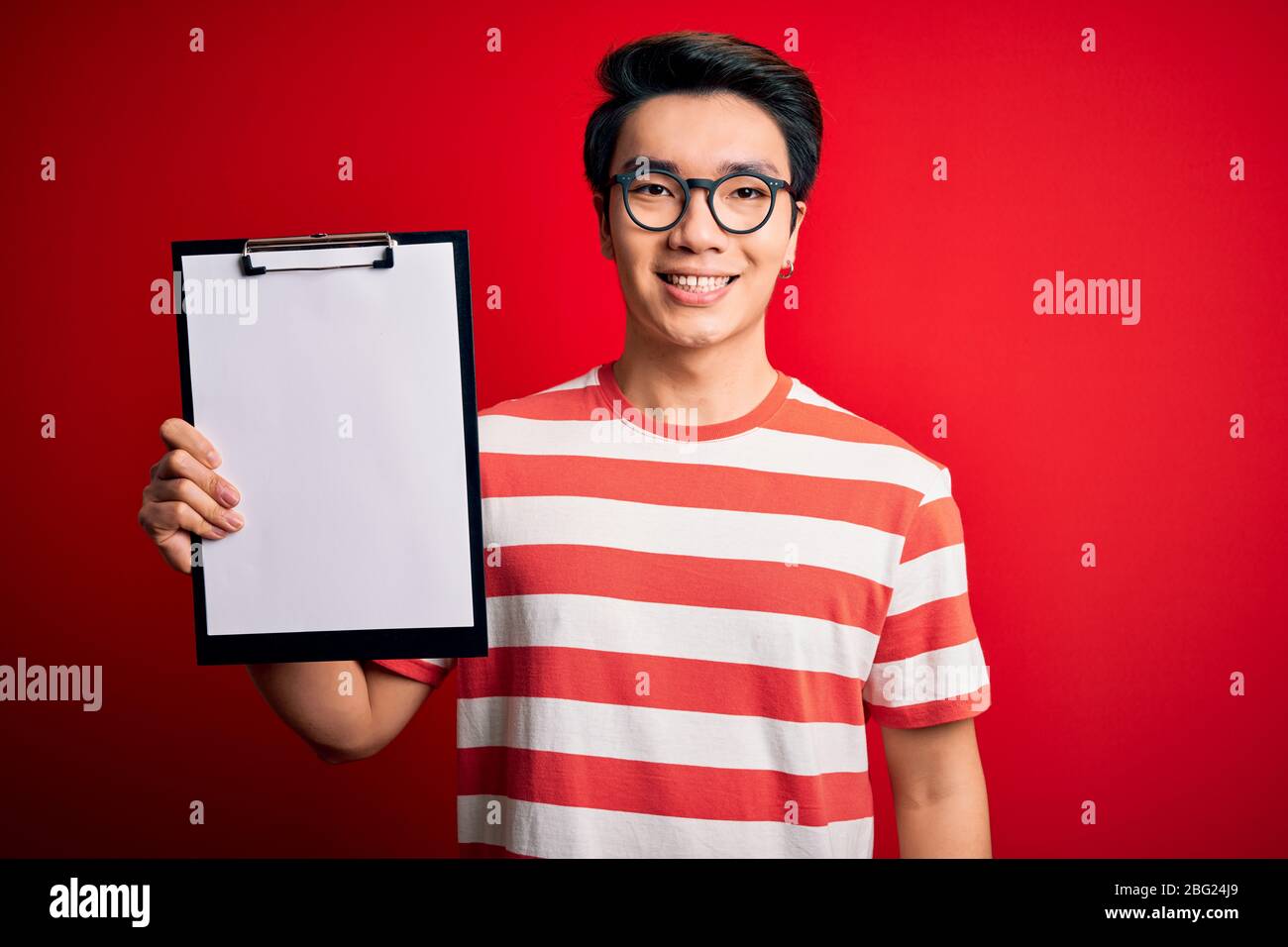 Young handsome chinese inspector man wearing glasses holding clipboard ...