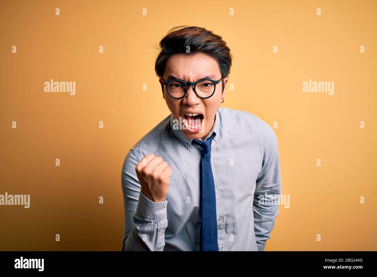 Young handsome chinese businessman wearing glasses and tie over yellow ...