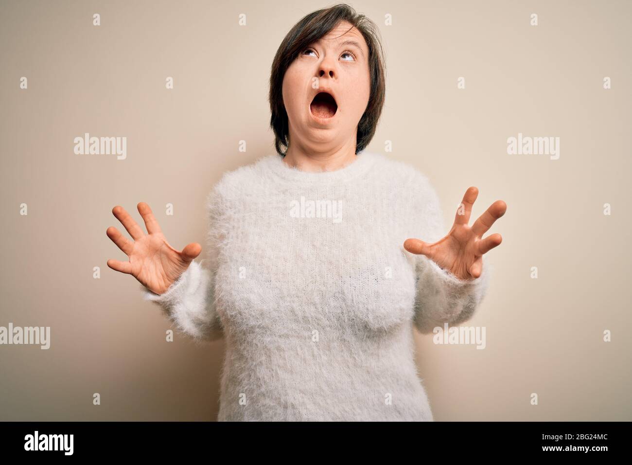 Young down syndrome woman standing over isolated background crazy and ...