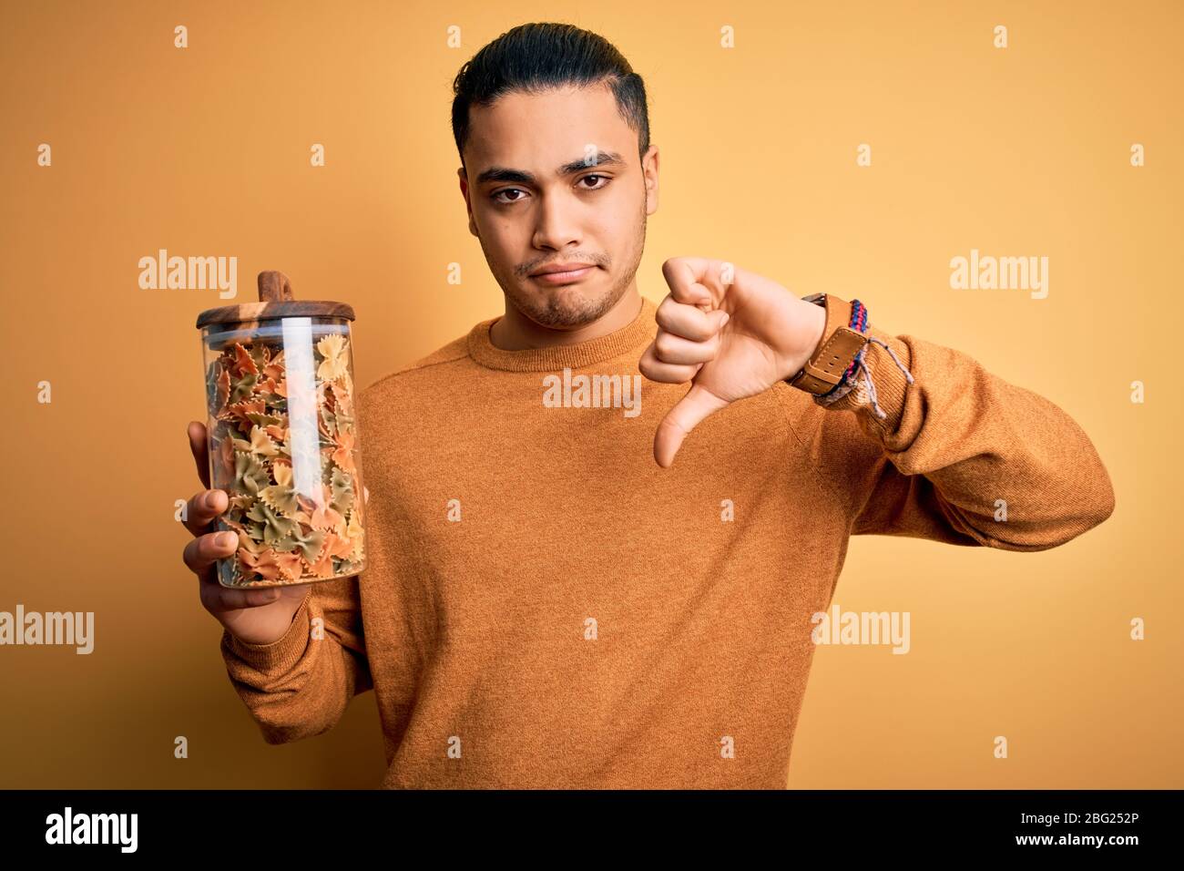 Young brazilian man holding jar with Italian dry pasta over isolated ...