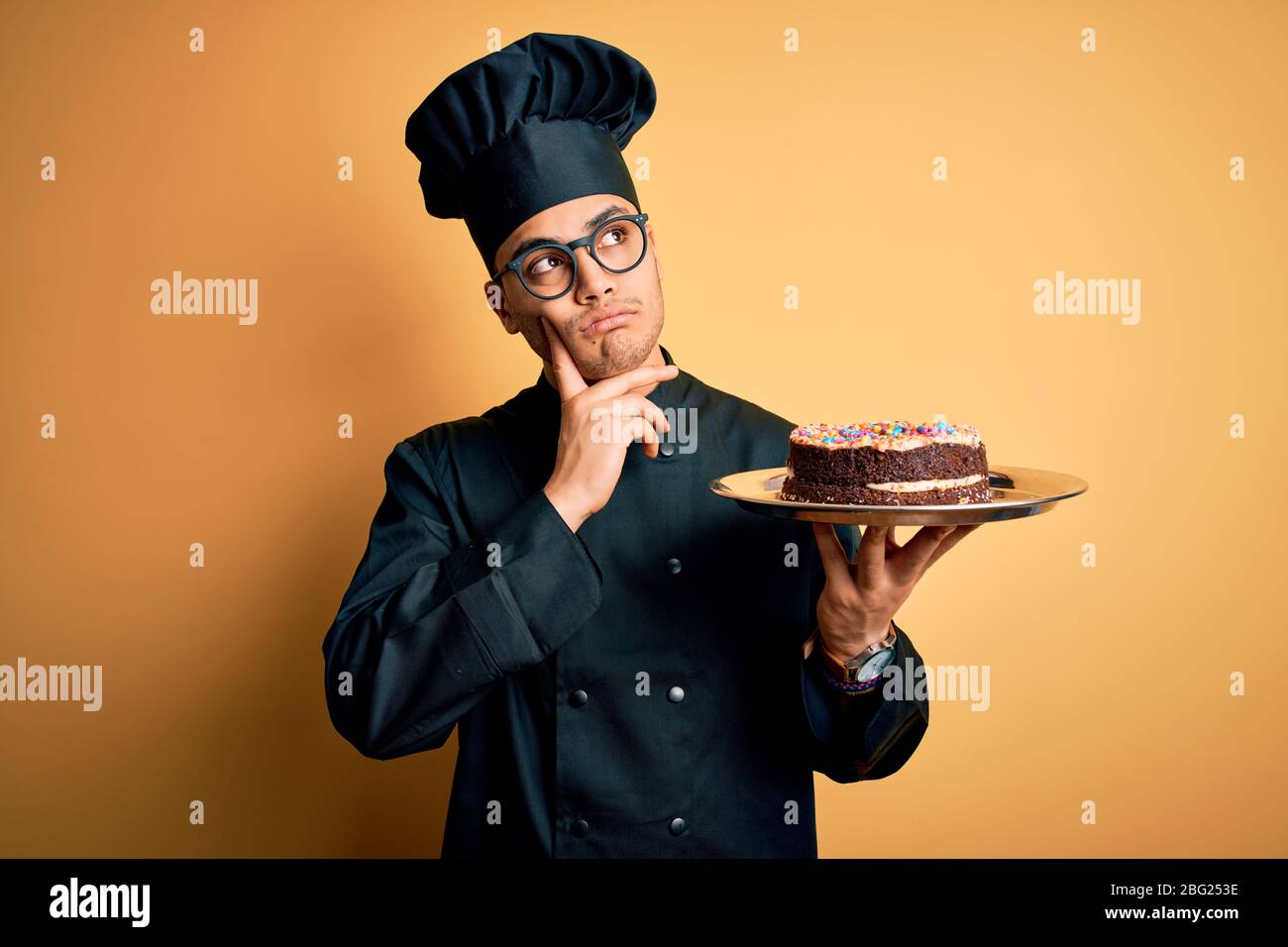 Young brazilian baker man wearing cooker uniform and hat holding tray ...