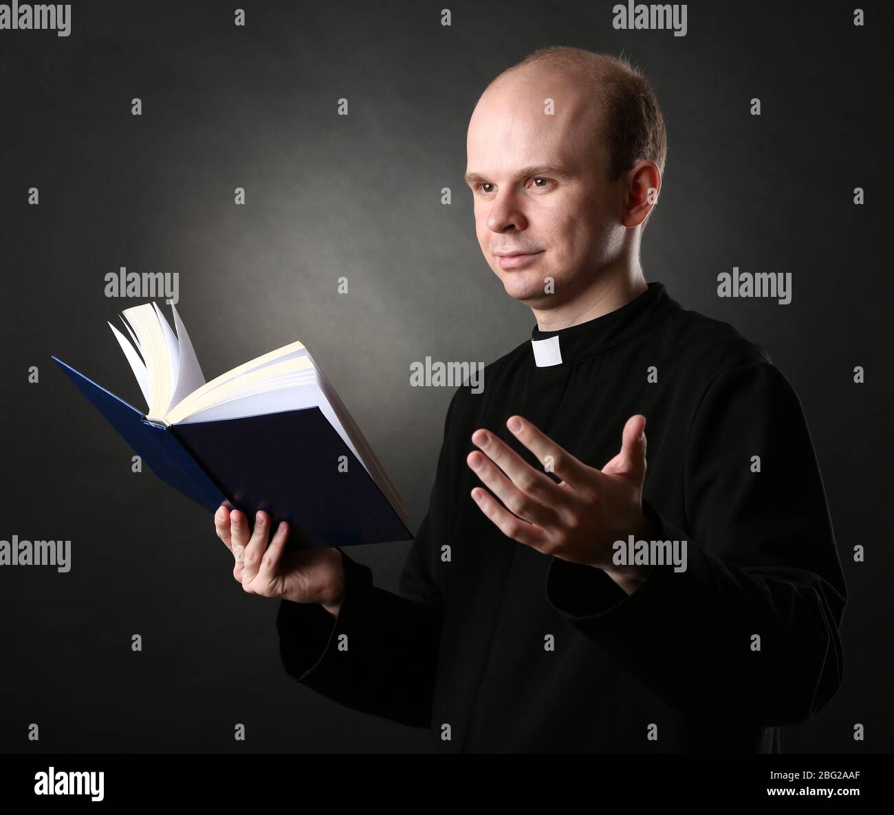 Priest with Holly Bible on black background Stock Photo - Alamy