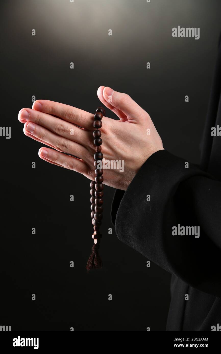 Priest holding rosary, on black background Stock Photo - Alamy