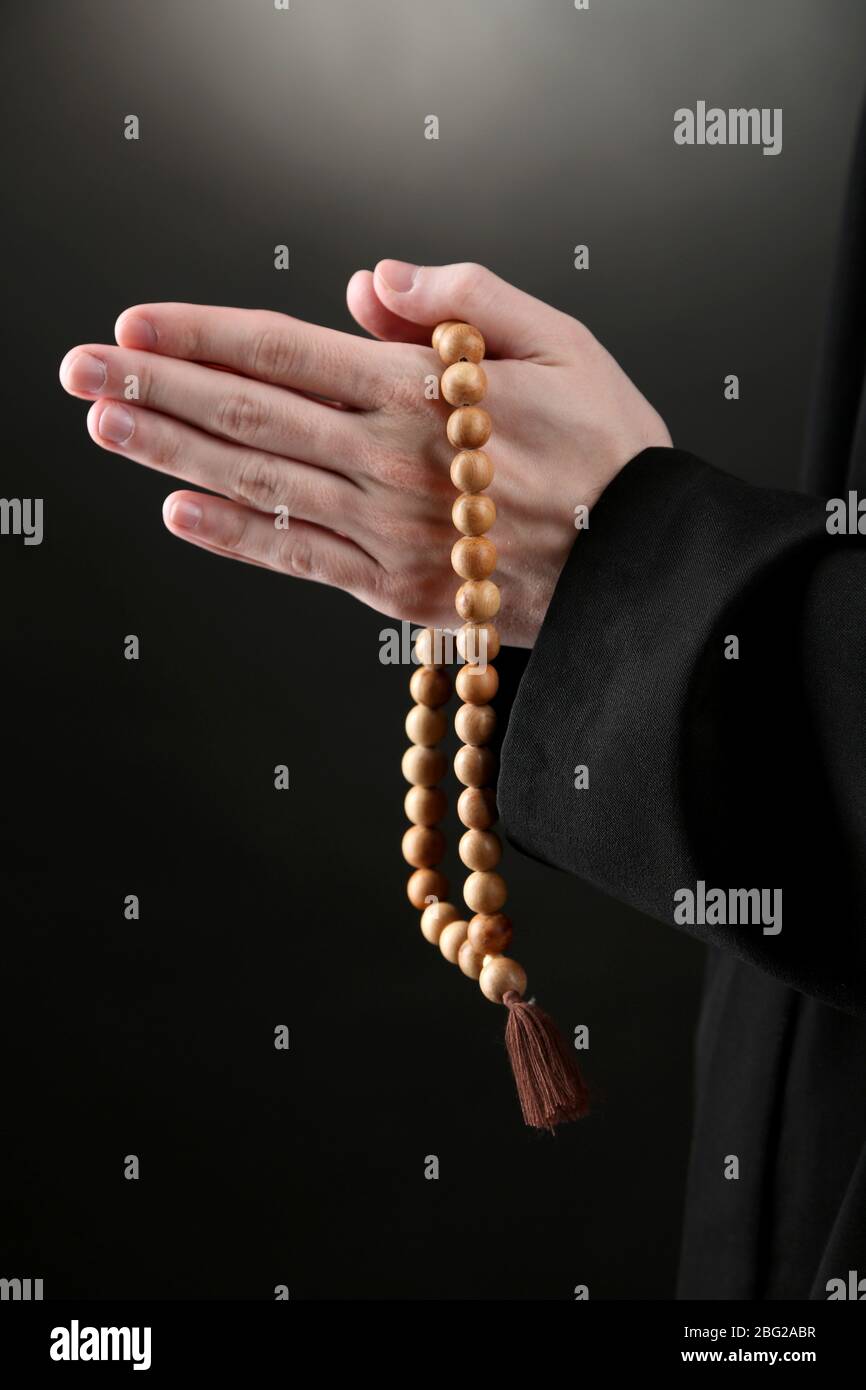 Priest holding rosary, on black background Stock Photo - Alamy
