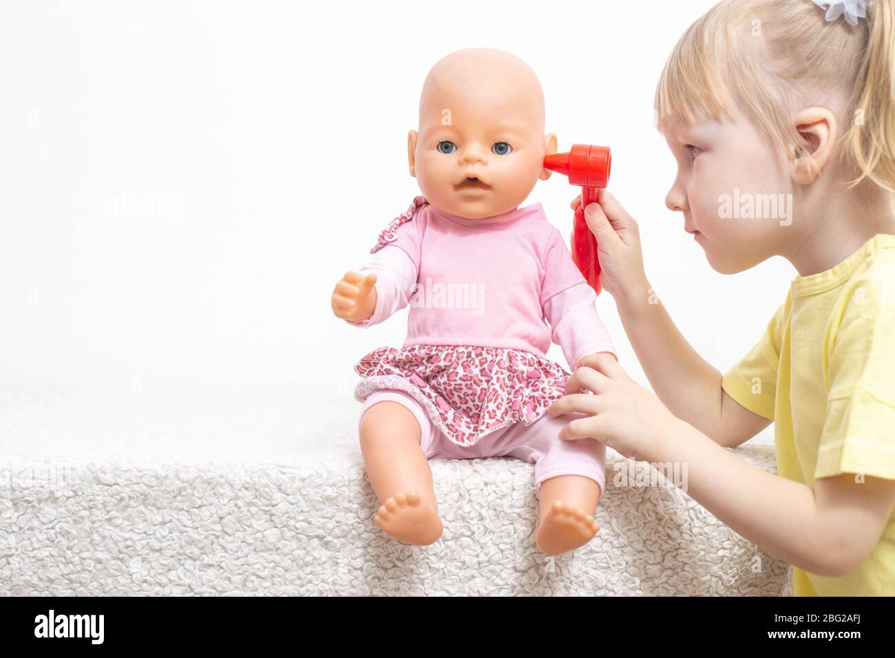 A little girl plays with a doll examines her ears. The concept of ...