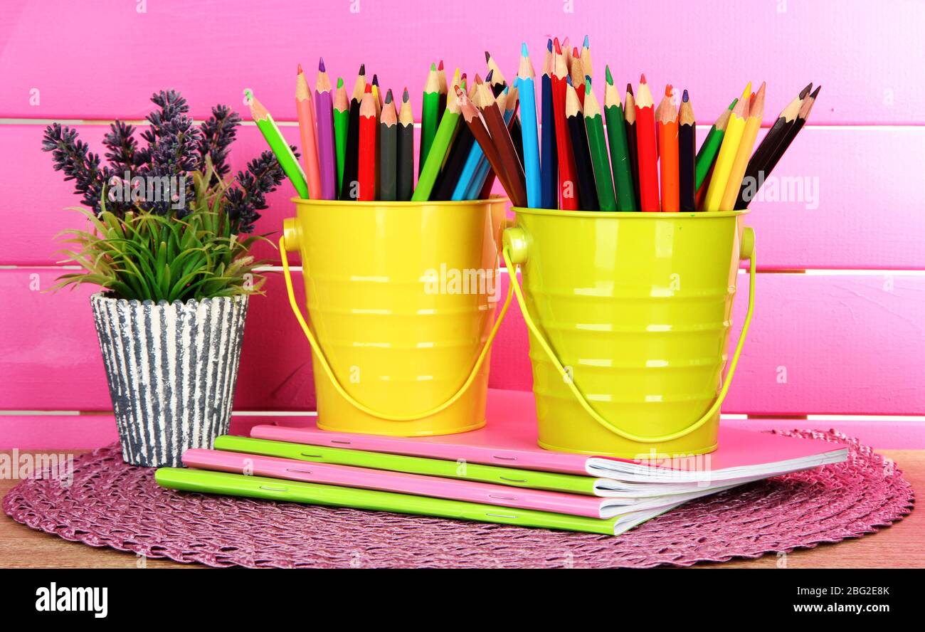 Colorful pencils in pails with copybooks on table on pink background ...