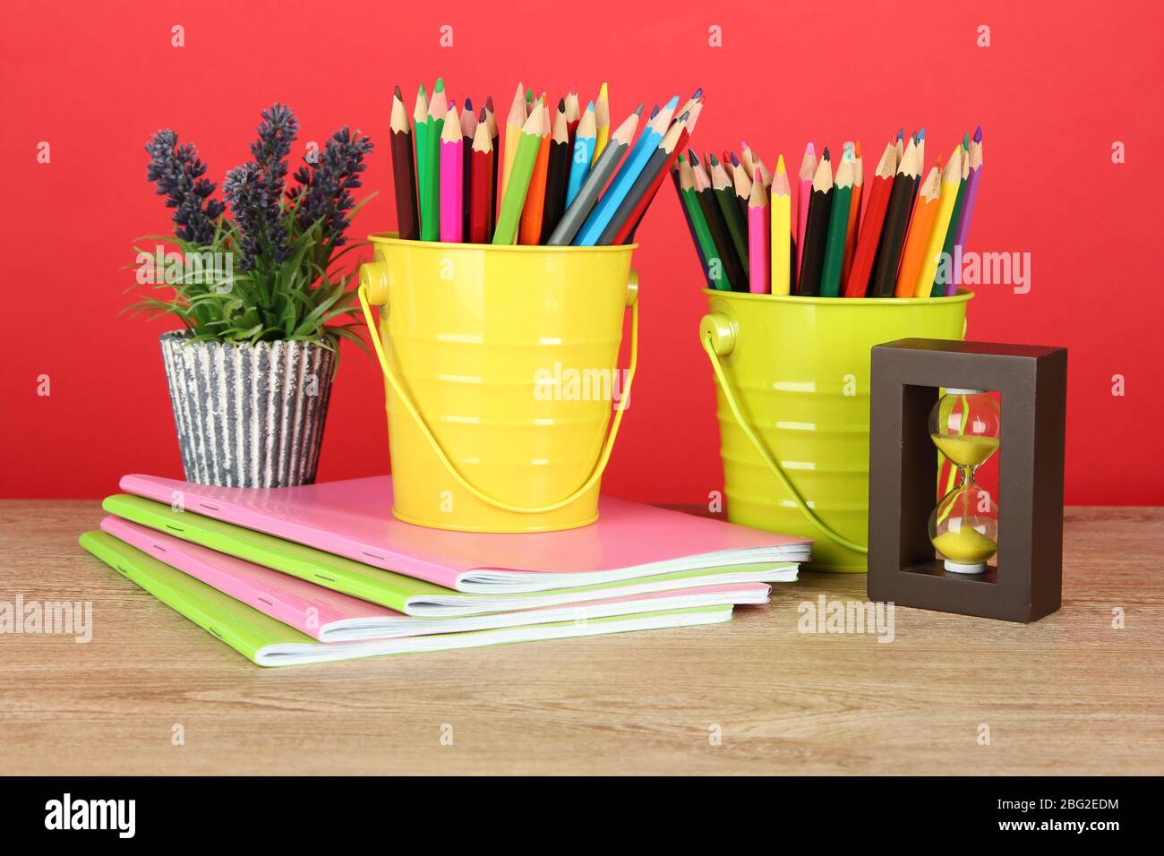 Colorful pencils in two pails with copybooks on table on red background ...