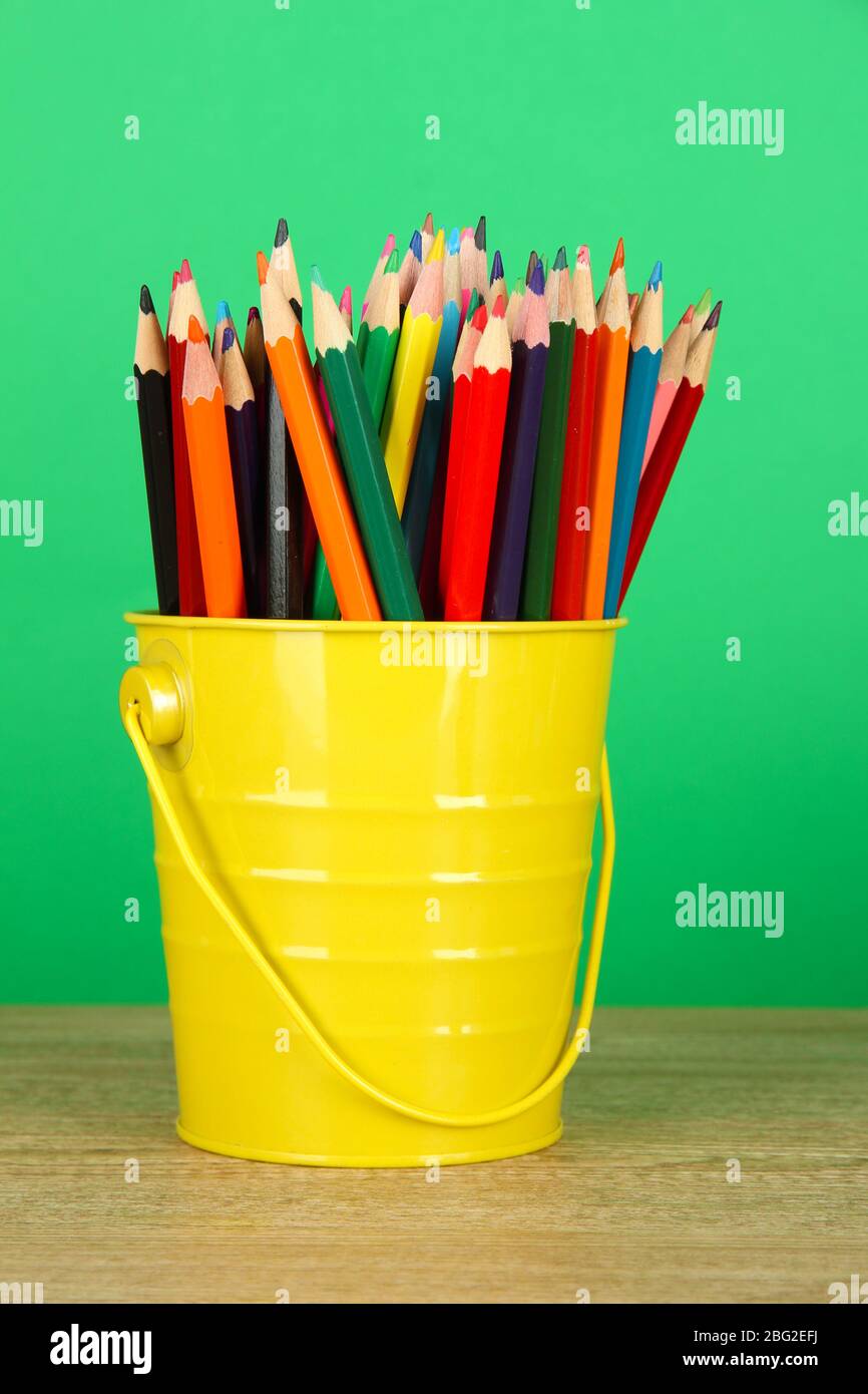 Colorful pencils in pail on table on green background Stock Photo - Alamy