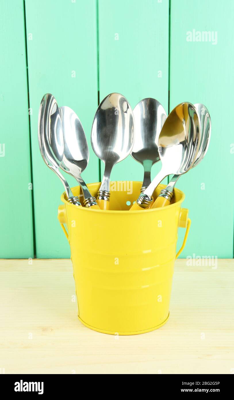 Spoons in metal bucket on color wooden background Stock Photo - Alamy
