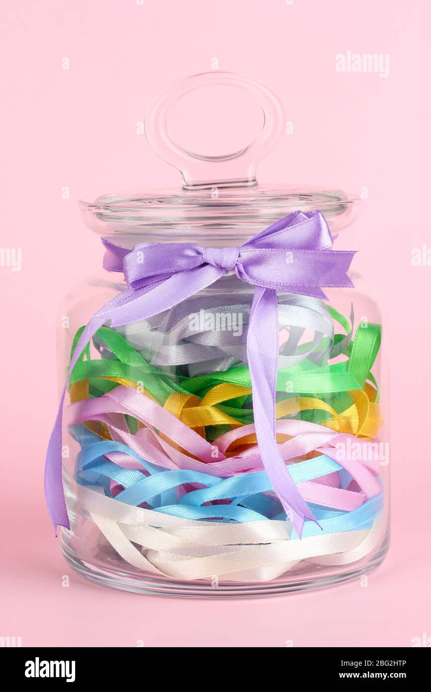 Glass jar containing various colored ribbons on pink background Stock ...