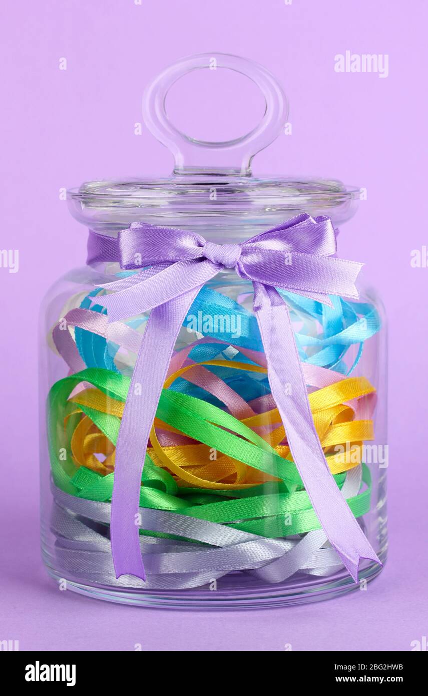 Glass jar containing various colored ribbons on lilac background Stock ...