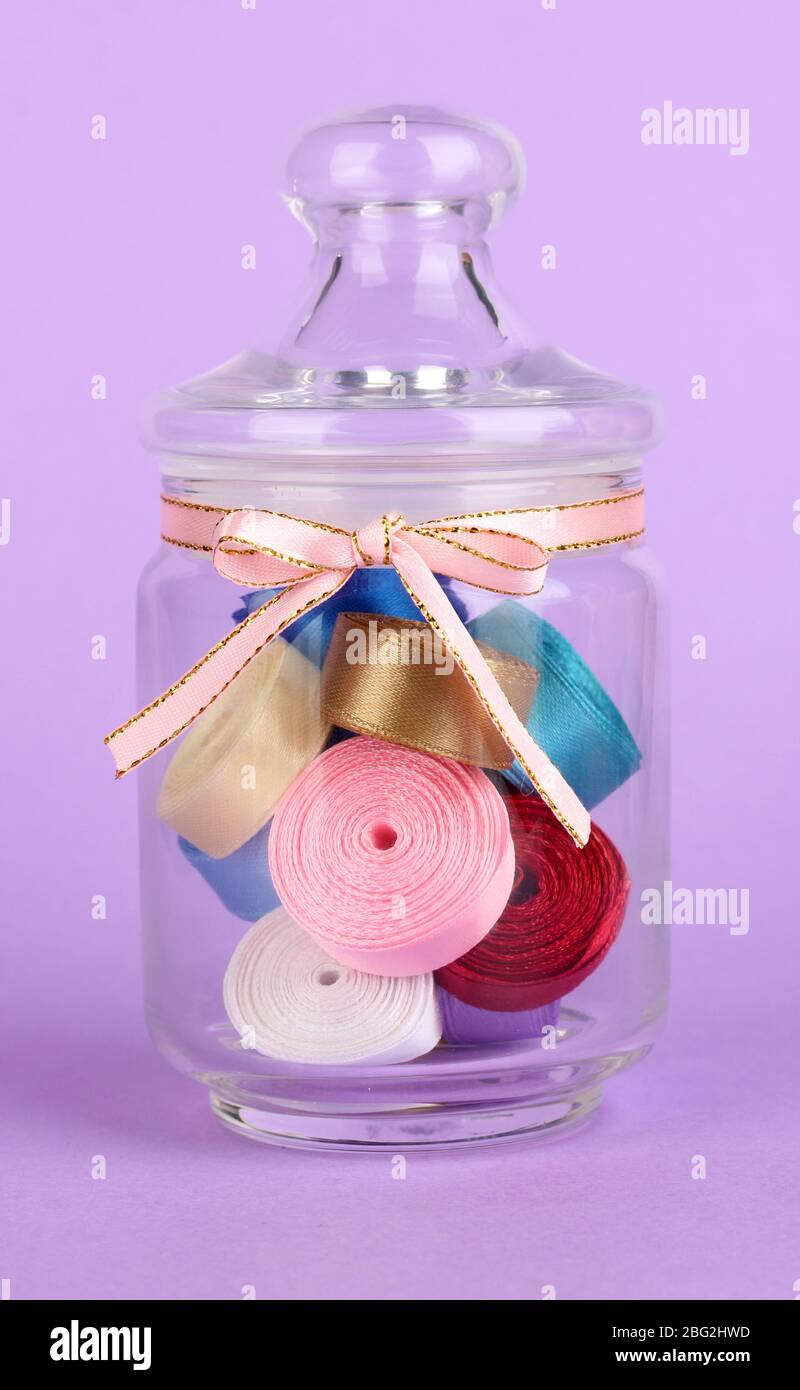 Glass jar containing various colored ribbons on lilac background Stock ...