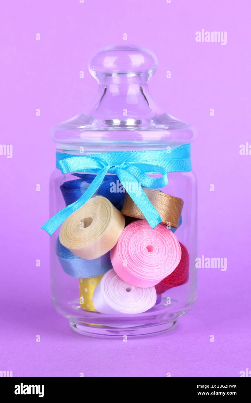 Glass jar containing various colored ribbons on lilac background Stock ...