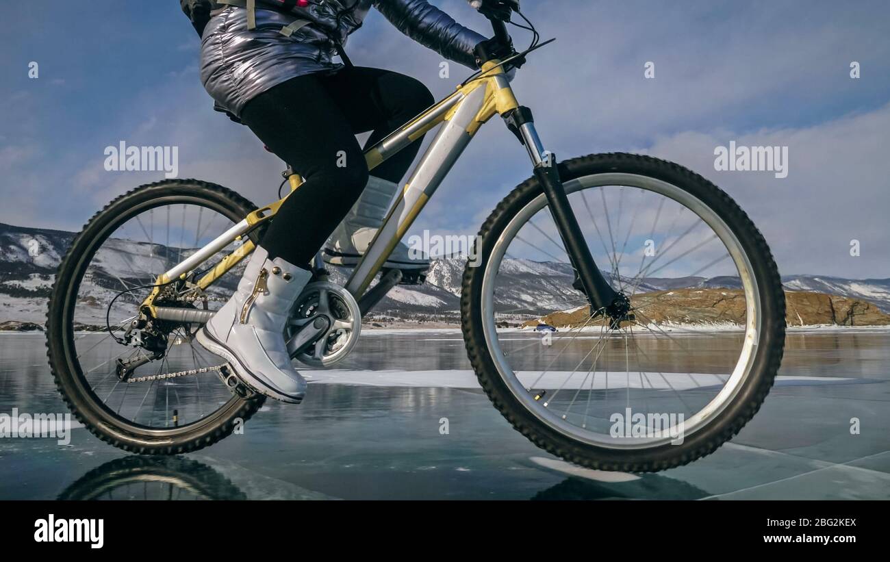 Woman is riding bicycle on the ice. Tires on bike are covered wi Stock ...