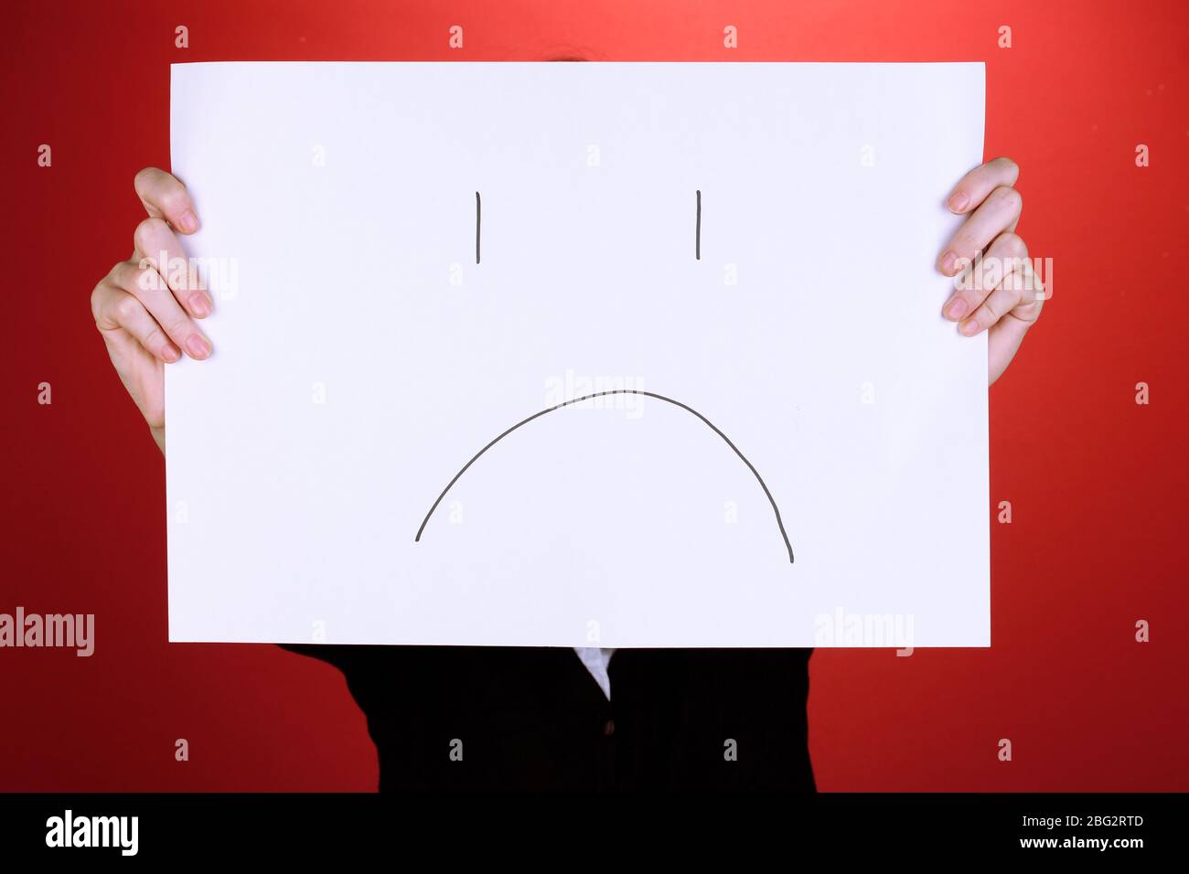 Woman holding paper with sad emoticon, on color background Stock Photo ...