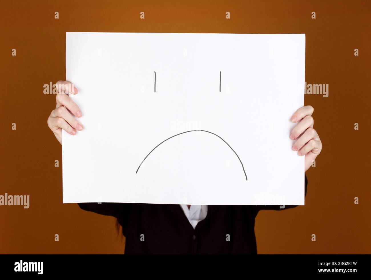 Woman holding paper with sad emoticon, on color background Stock Photo ...