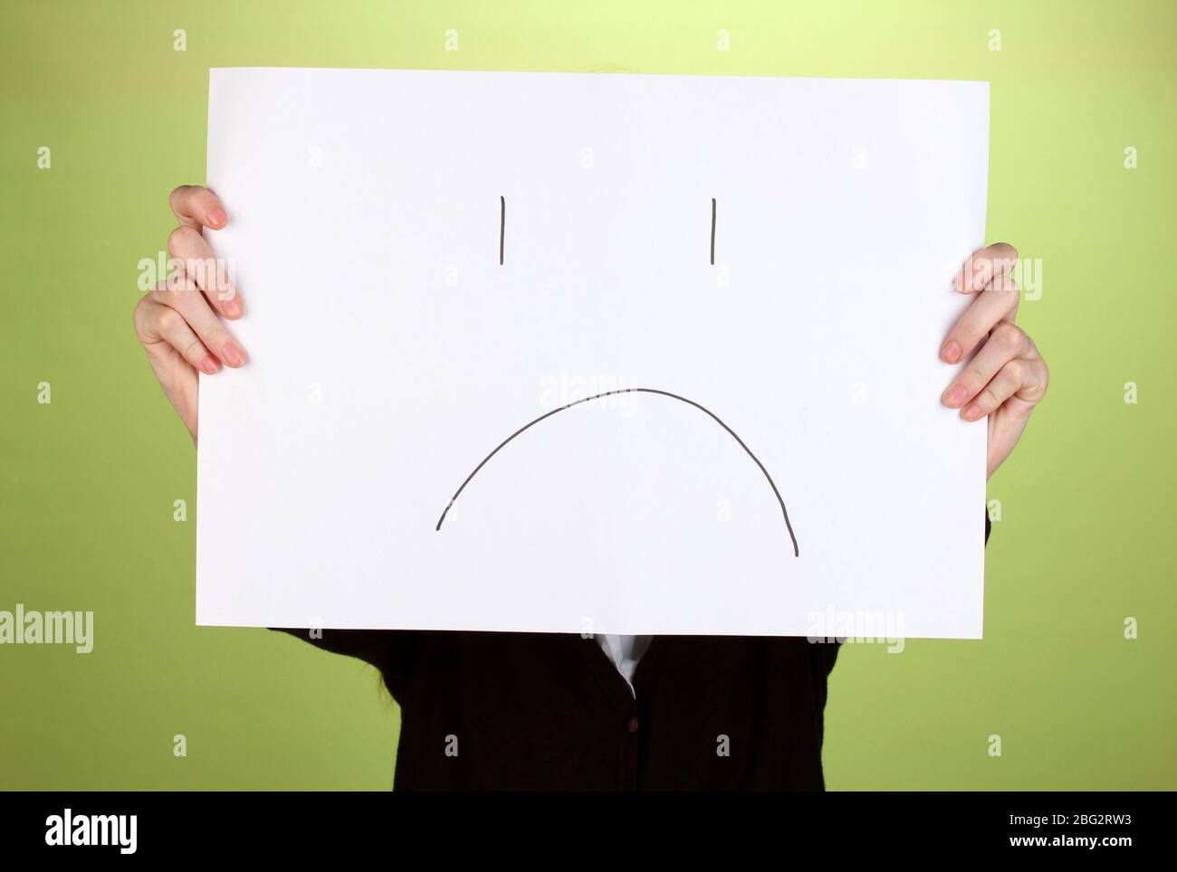 Woman holding paper with sad emoticon, on color background Stock Photo ...
