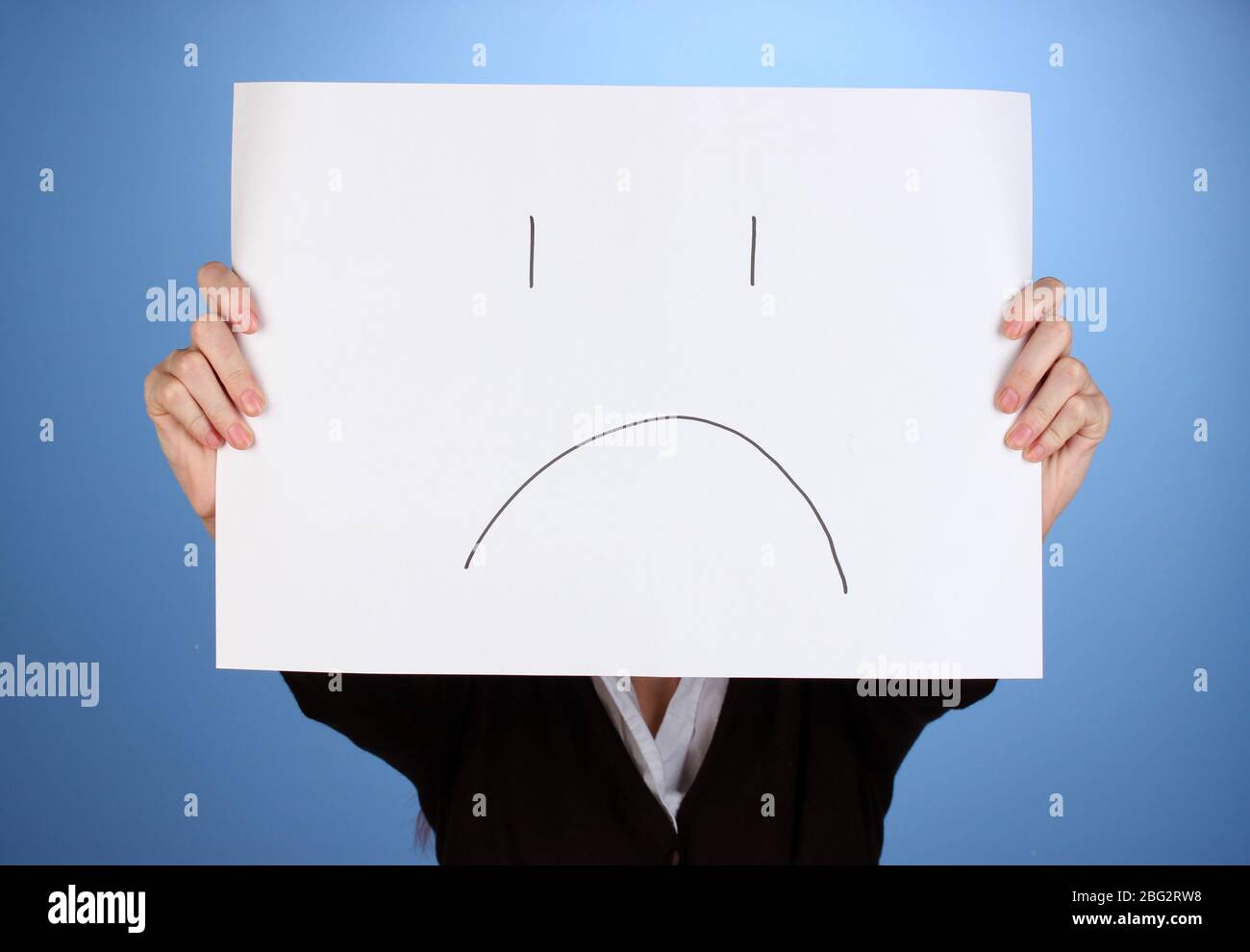 Woman holding paper with sad emoticon, on color background Stock Photo ...