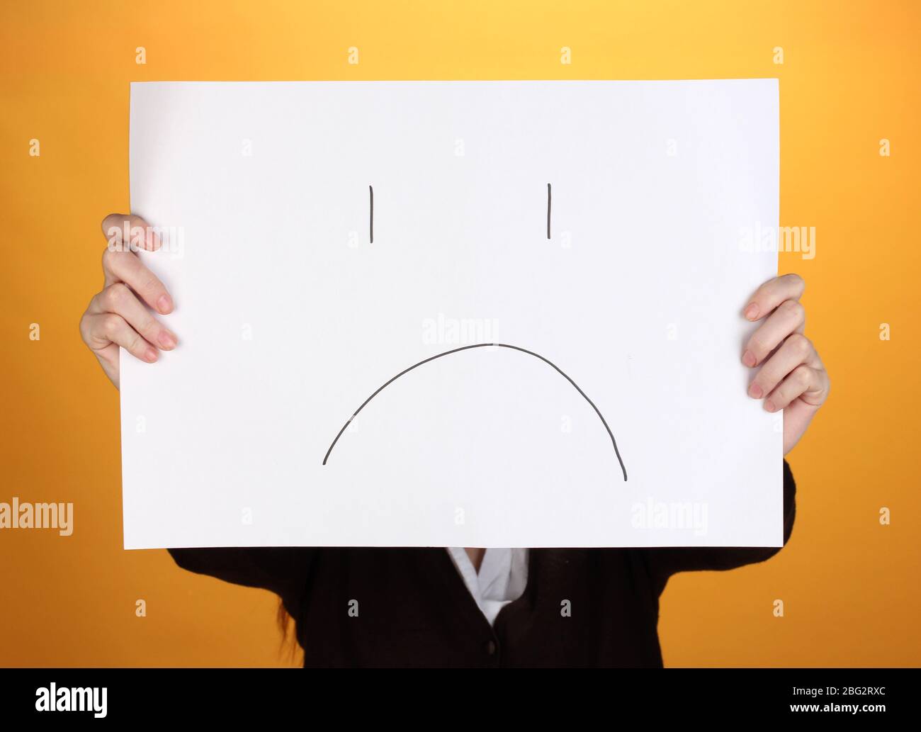 Woman holding paper with sad emoticon, on color background Stock Photo ...