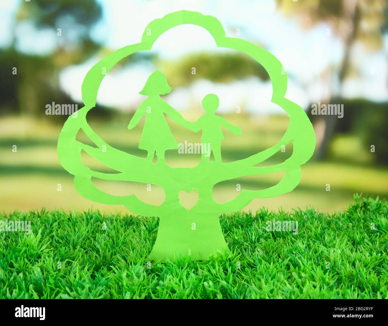 Green cut out paper tree with people inside, on green grass on bright ...